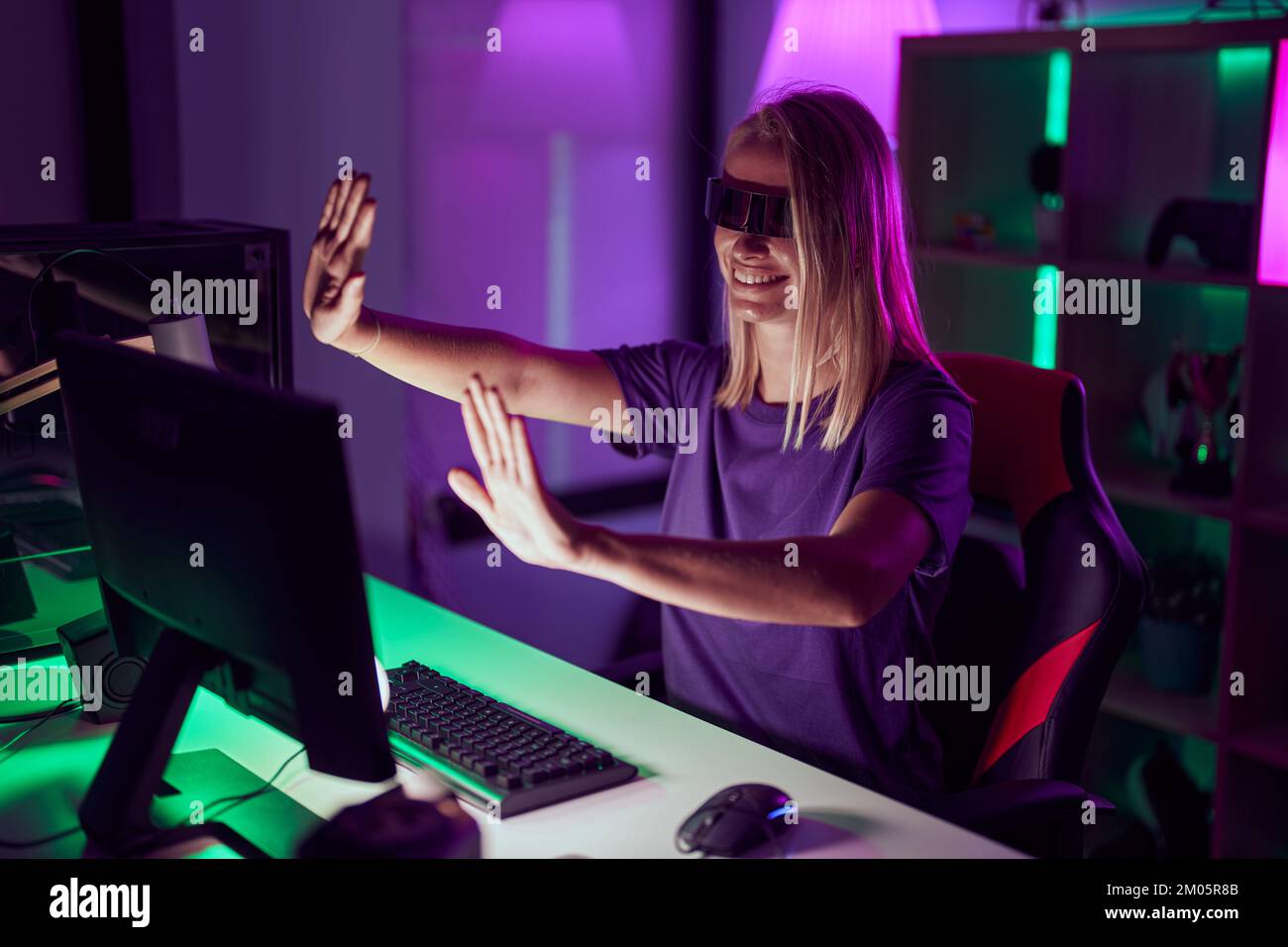 Young blonde woman streamer using virtual reality glasses at gaming ...
