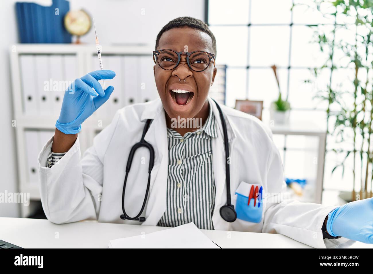 Young african doctor man holding syringe at the hospital angry and mad ...