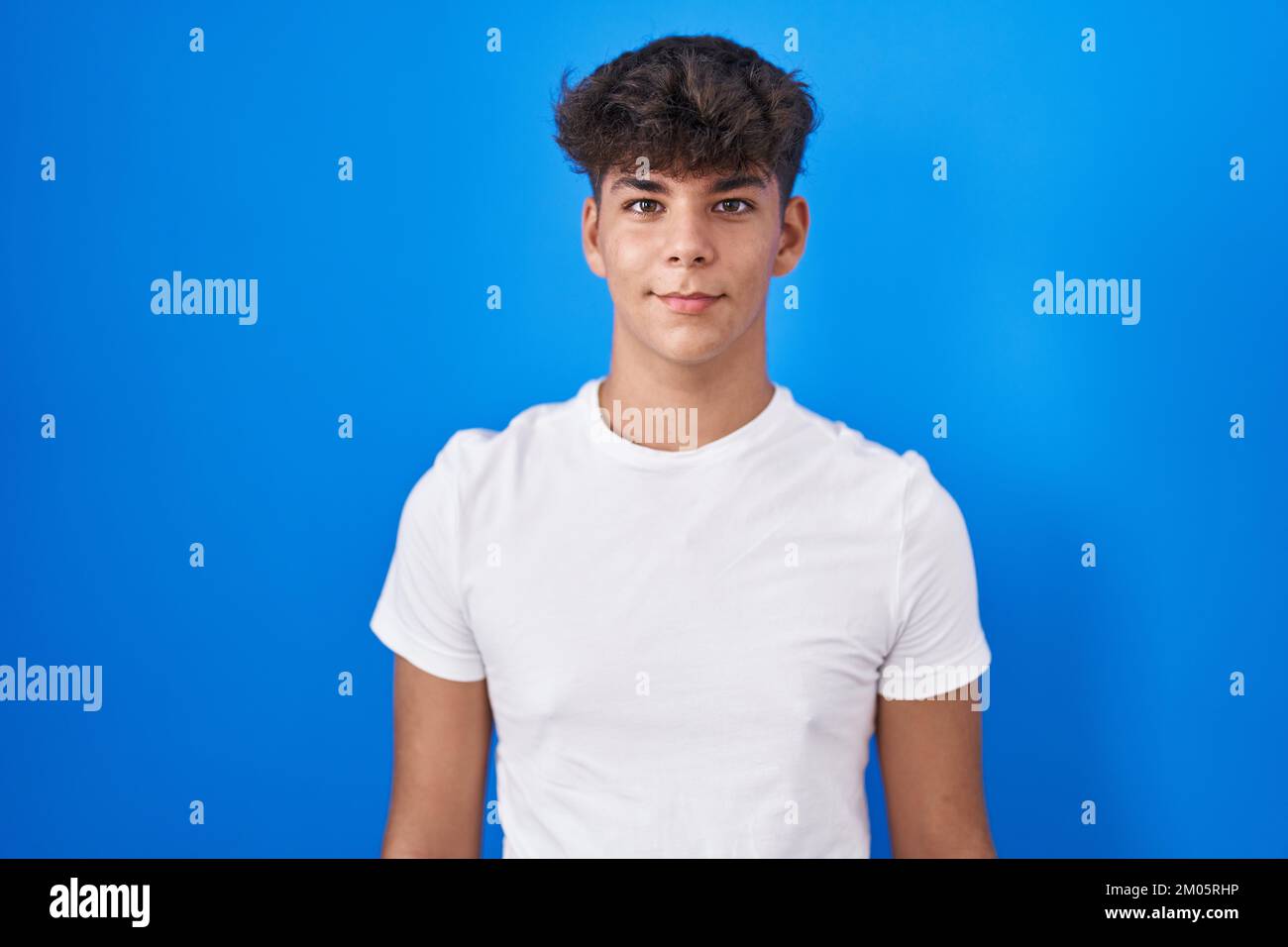Hispanic teenager standing over blue background with a happy and cool ...