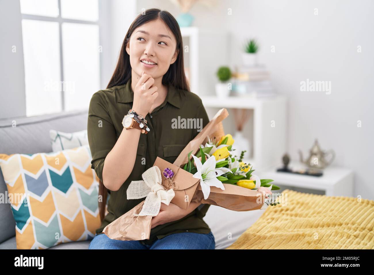 Chinese young woman holding bouquet of white flowers with hand on chin ...
