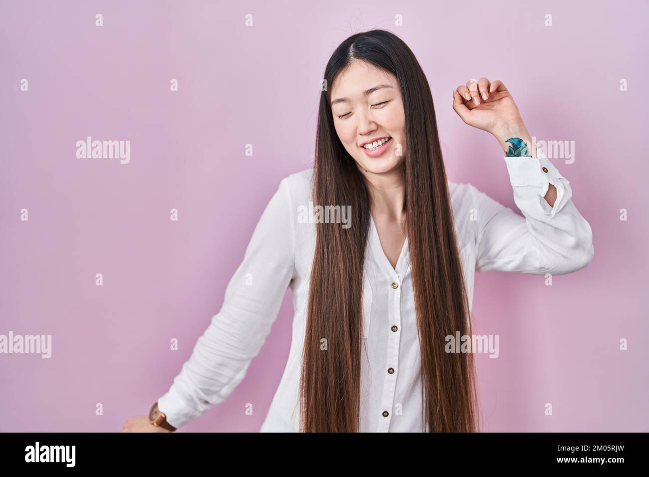 Chinese young woman standing over pink background dancing happy and ...