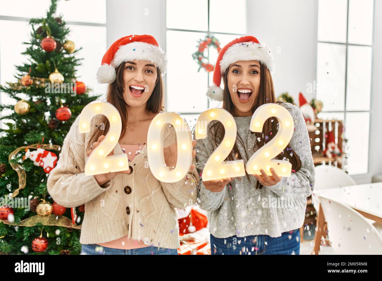 Two women celebrate new year holding 2022 lights standing by christmas ...