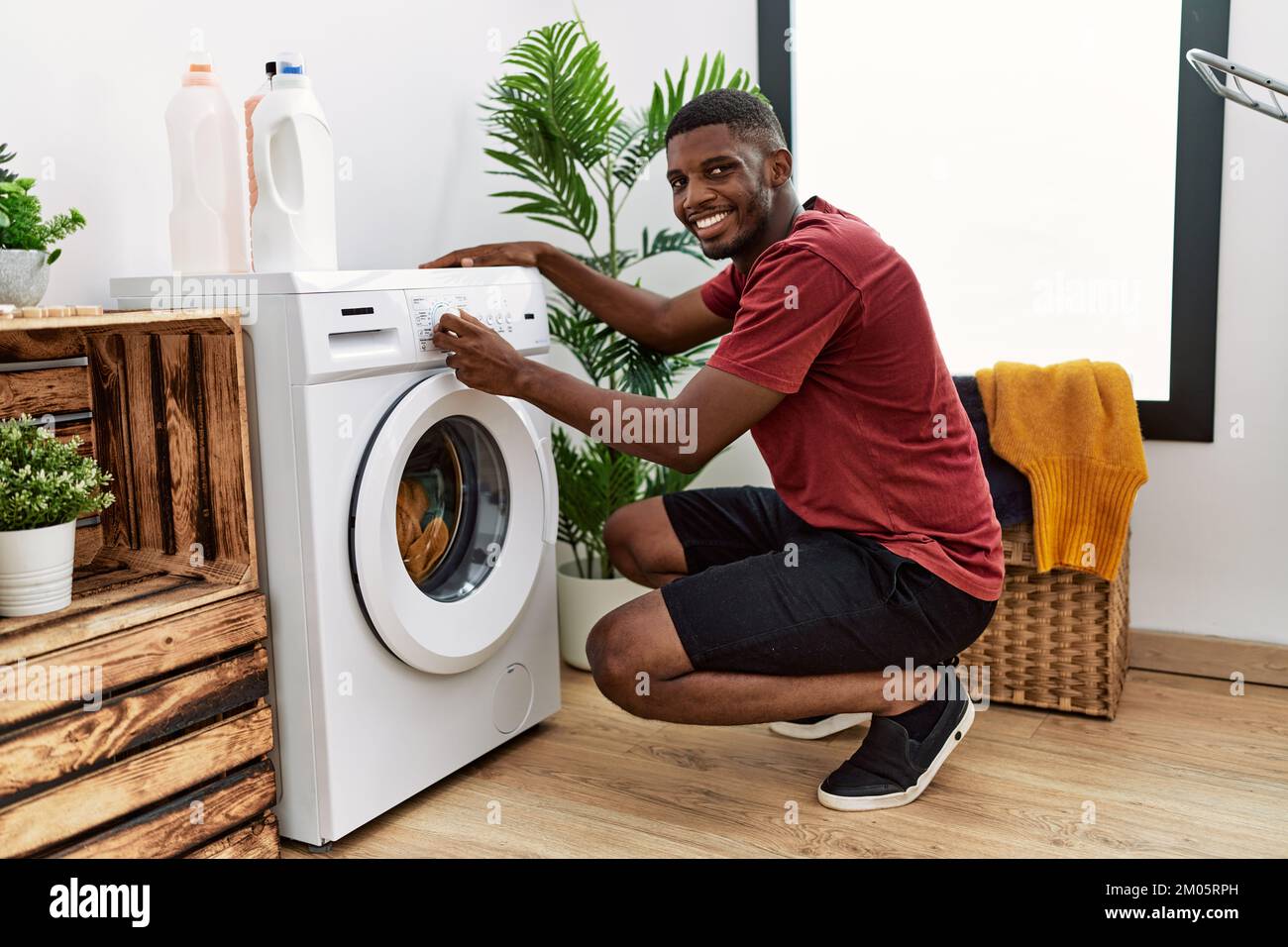 Young african american man cleaning clothes using washing machine at ...