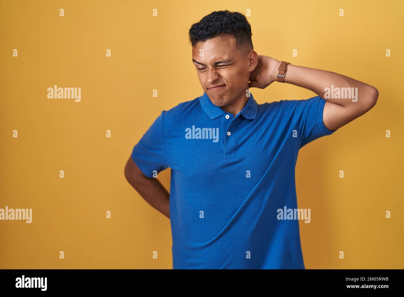 Young hispanic man standing over yellow background suffering of neck ...