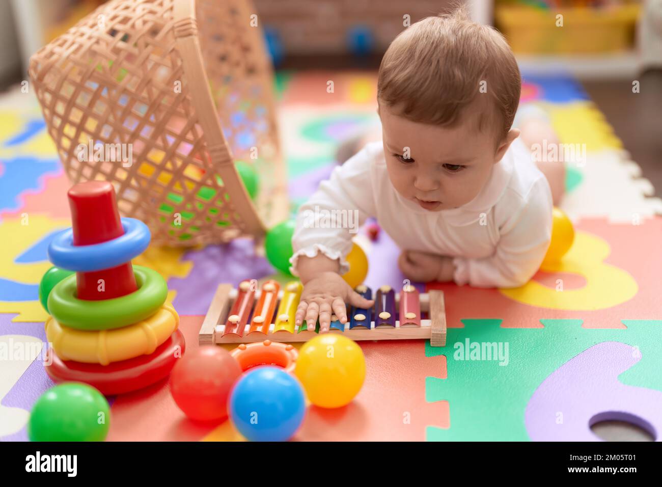 Adorable toddler touching xylophone lying on floor at kindergarten ...