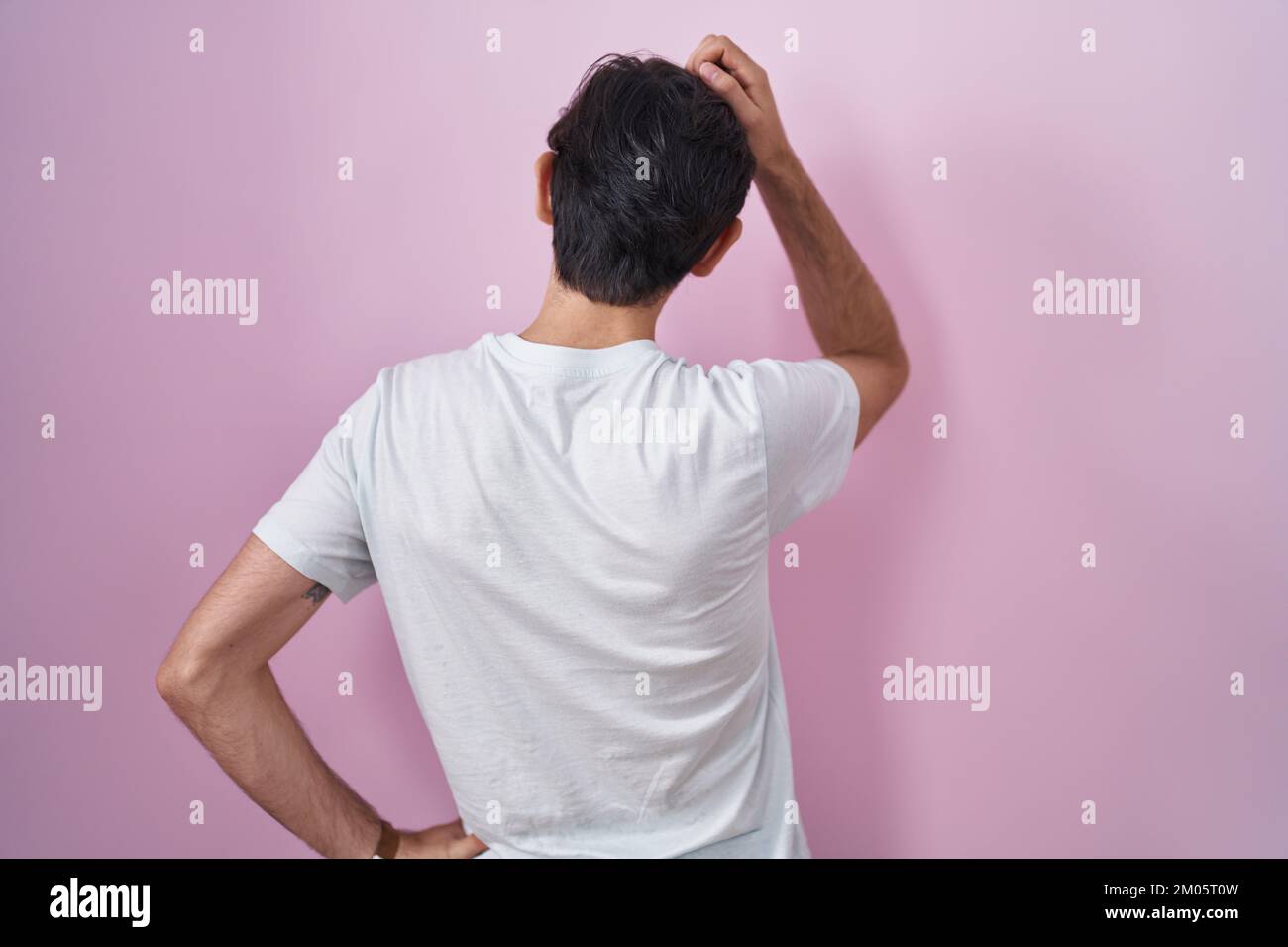 Young hispanic man standing over pink background backwards thinking ...