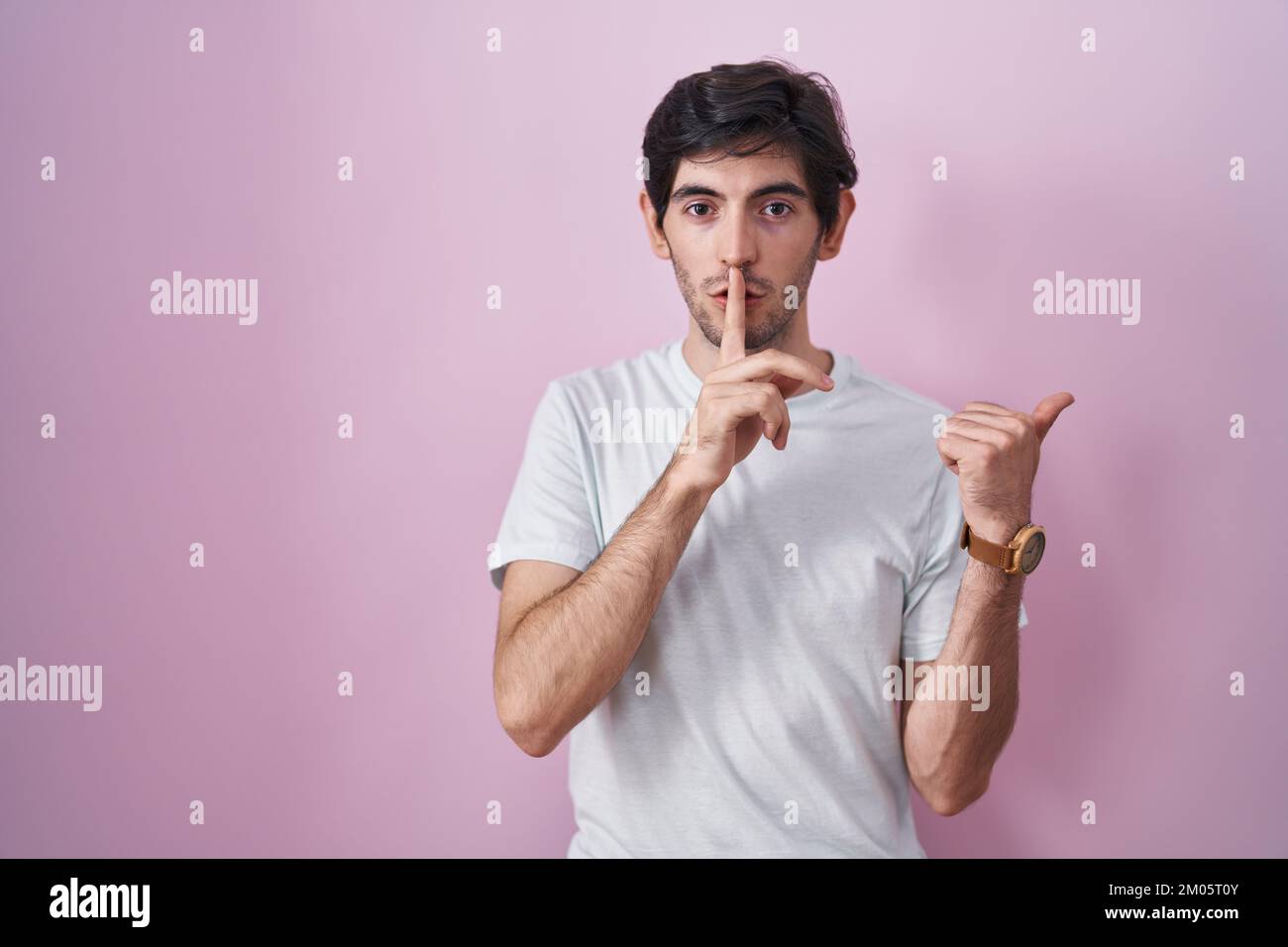 Young hispanic man standing over pink background asking to be quiet ...