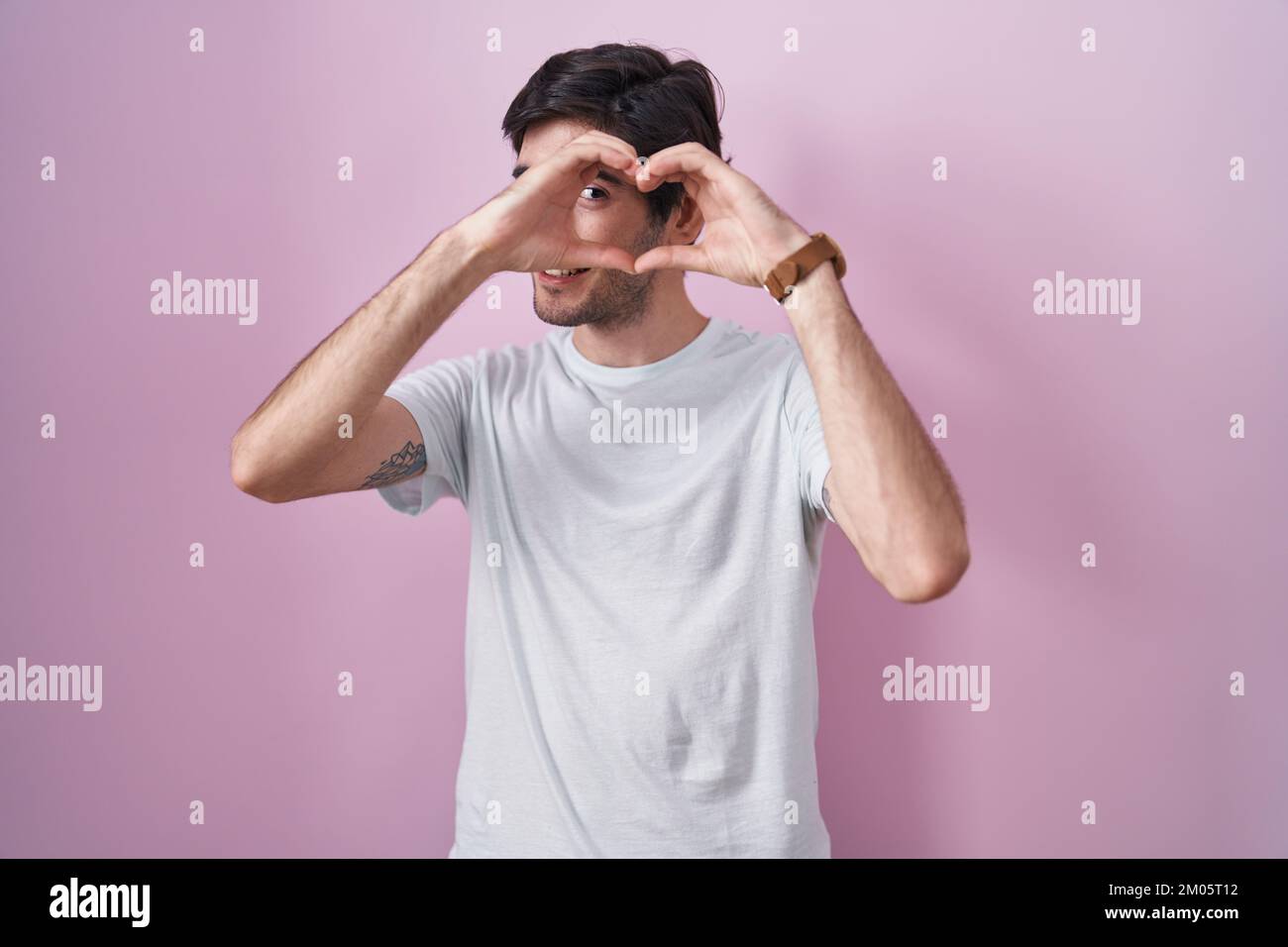 Young hispanic man standing over pink background doing heart shape with ...
