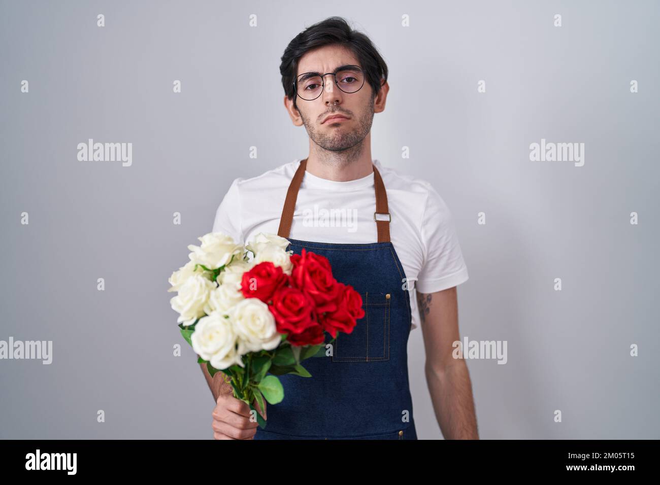 Young hispanic man holding bouquet of white and red roses depressed and ...