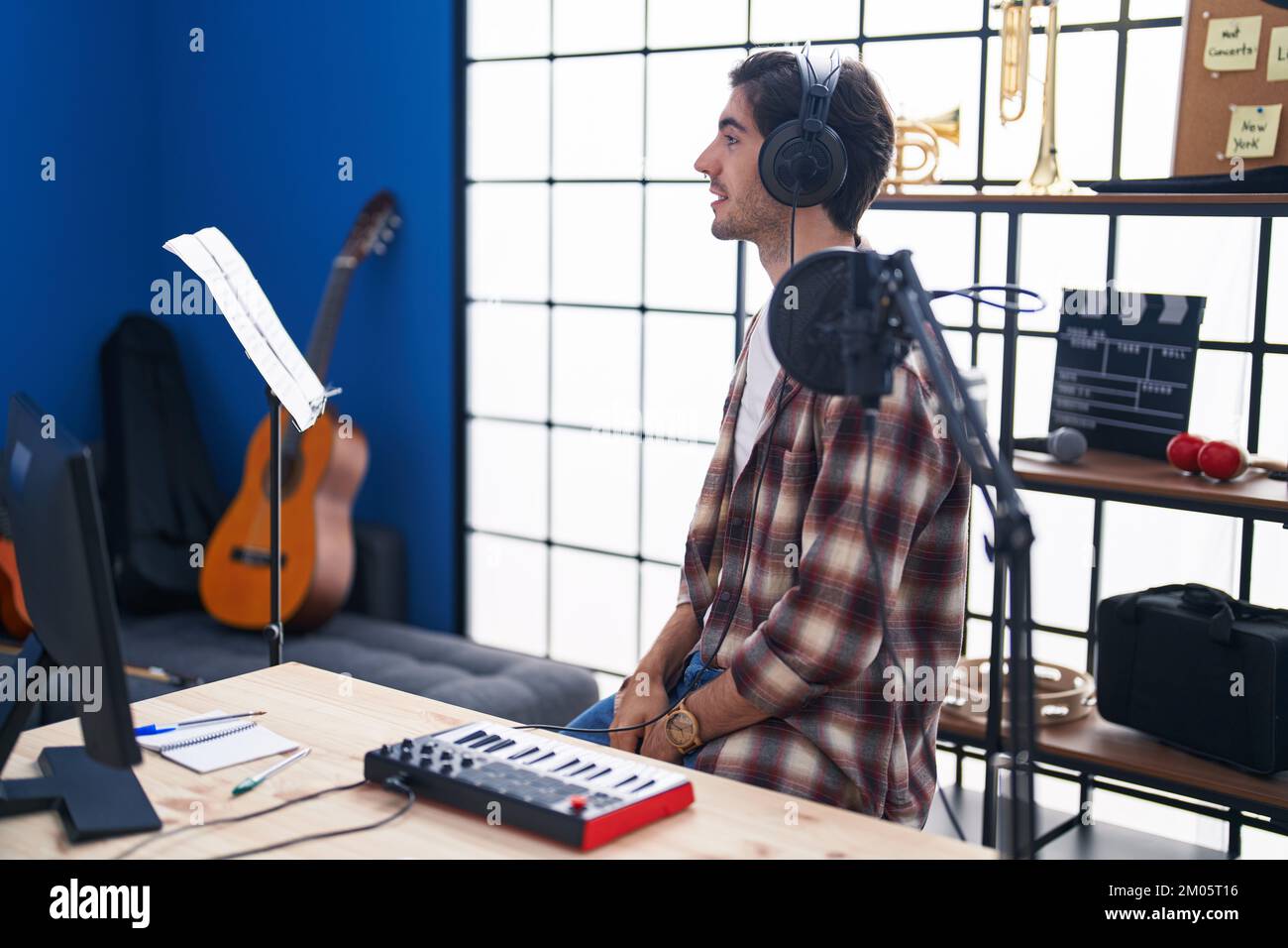 Young hispanic man playing piano at music studio looking to side, relax ...