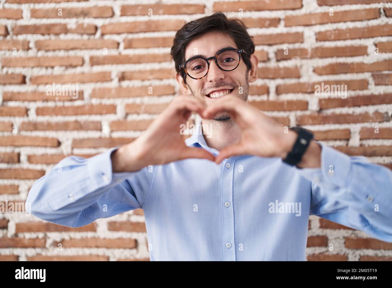 Young hispanic man standing over brick wall background smiling in love ...