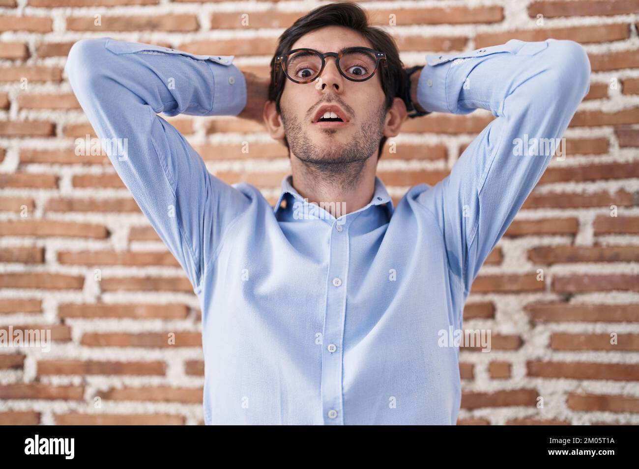 Young hispanic man standing over brick wall background crazy and scared ...