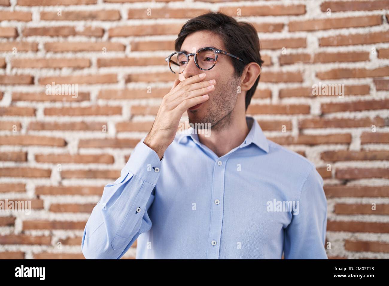 Young hispanic man standing over brick wall background bored yawning ...