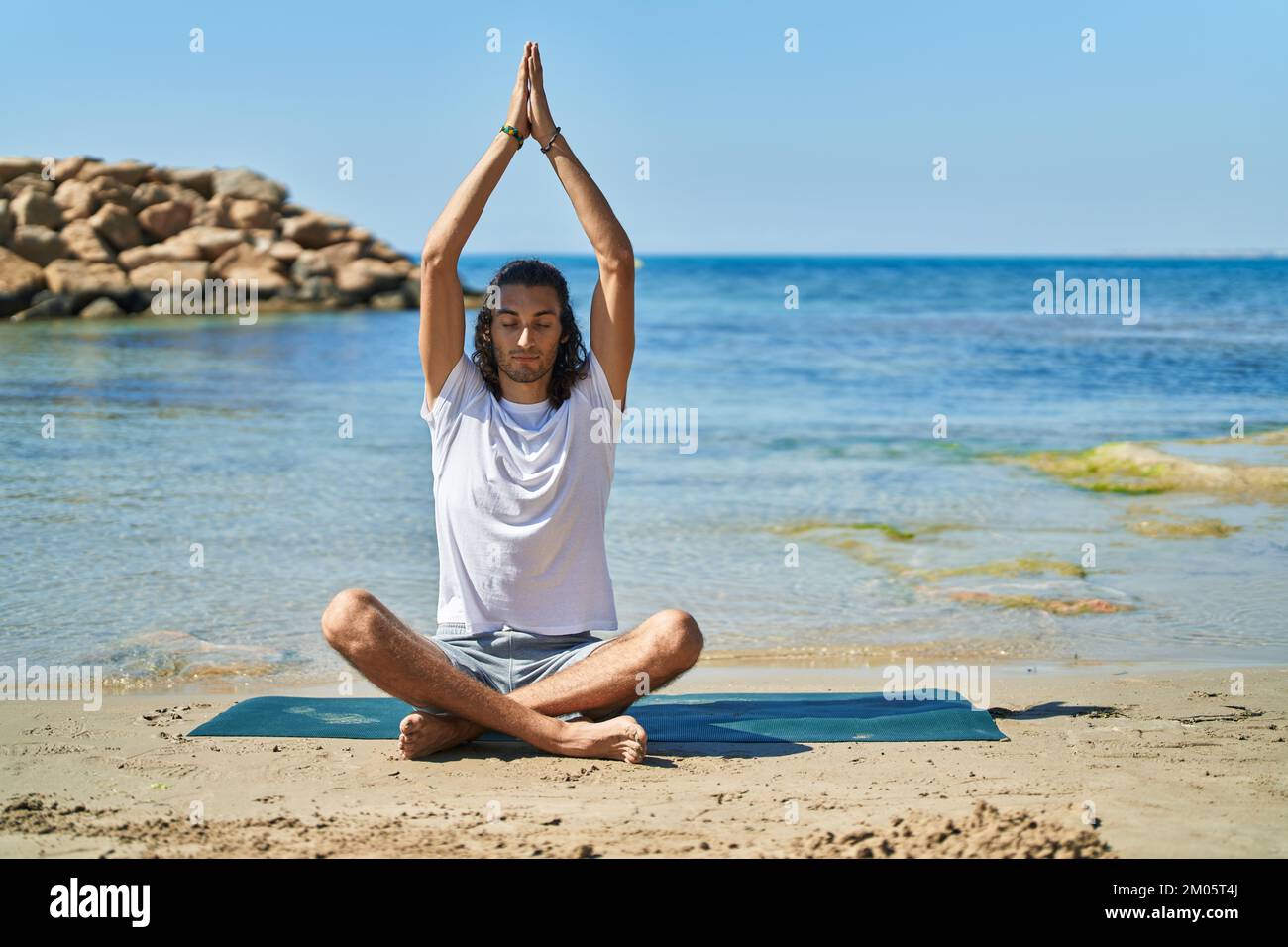 Young hispanic man doing yoga exercise sitting on sand at beach Stock ...