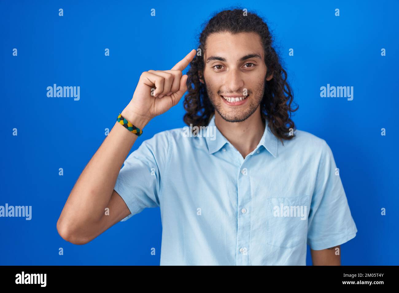 Young hispanic man standing over blue background smiling pointing to ...