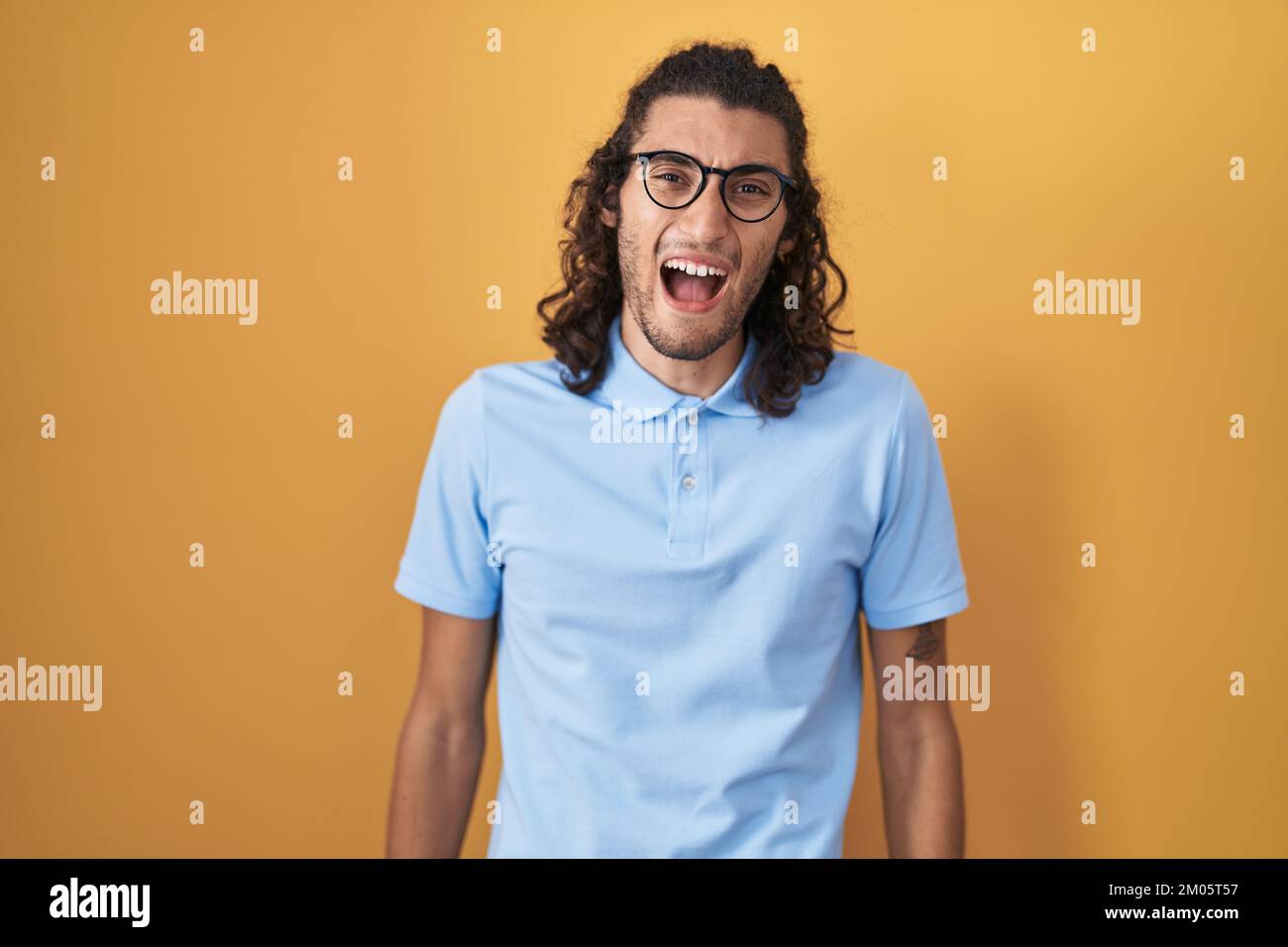 Young hispanic man standing over yellow background angry and mad ...