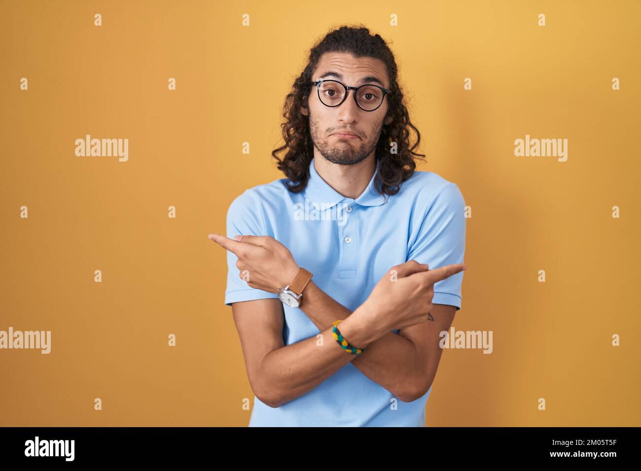Young hispanic man standing over yellow background pointing to both ...