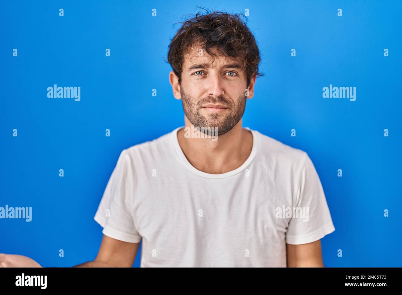Hispanic young man standing over blue background clueless and confused ...