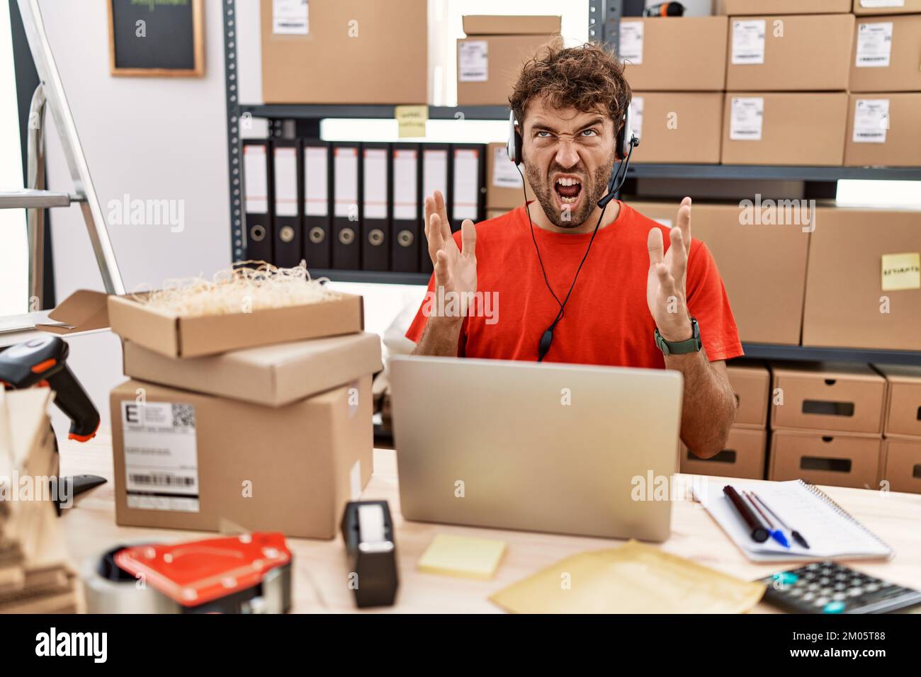 Young hispanic call center agent man working at warehouse crazy and mad ...