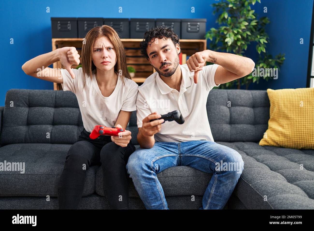 Young couple playing video game holding controller at home with angry ...