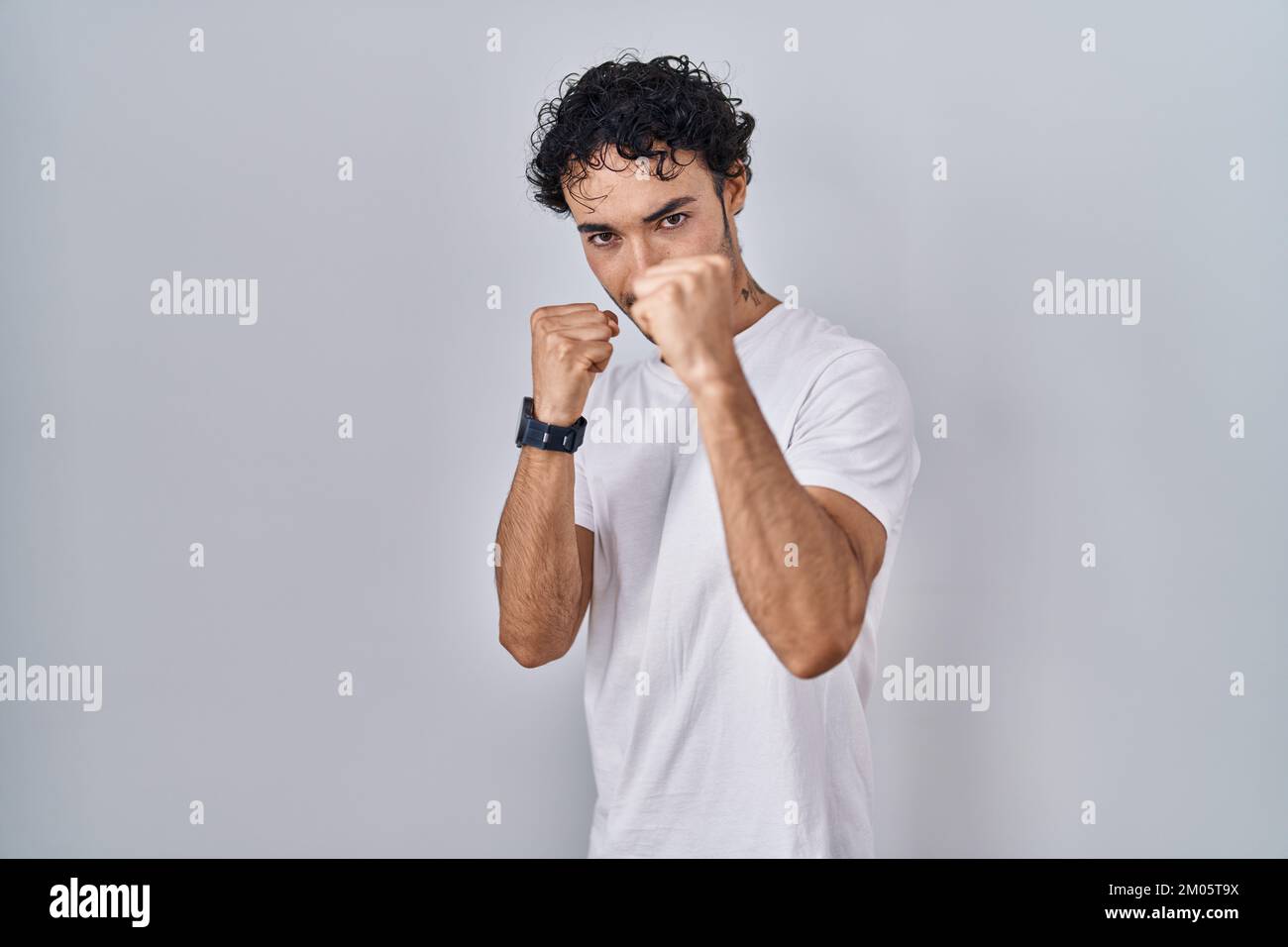 Hispanic man standing over isolated background ready to fight with fist ...