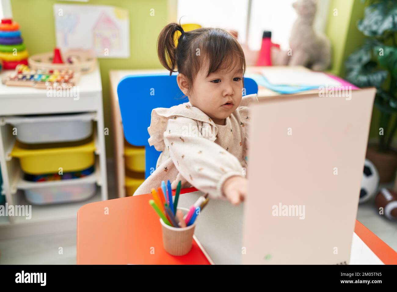 Adorable chinese girl preschool student sitting on table opening ...