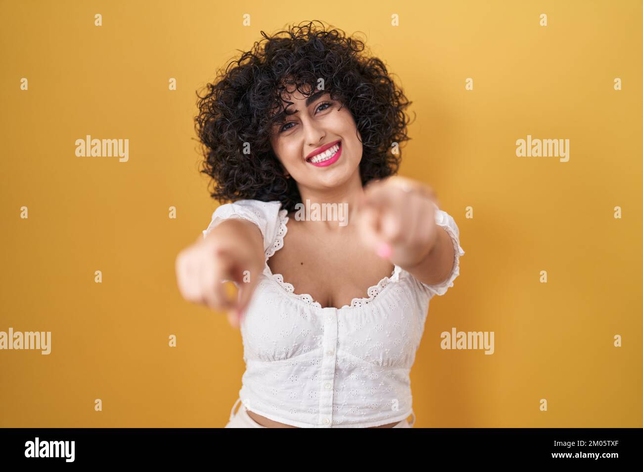 Young brunette woman with curly hair standing over yellow background ...