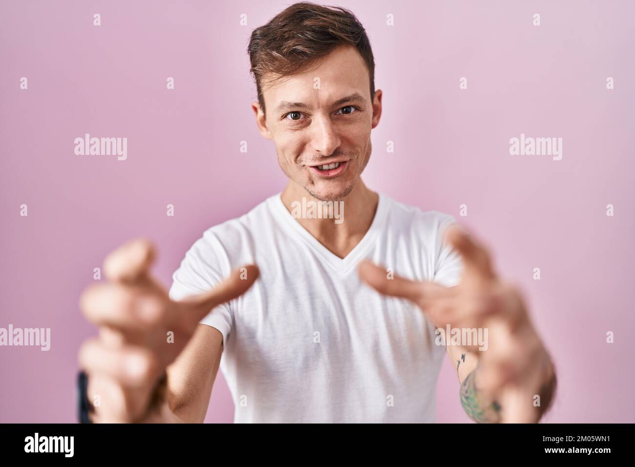 Caucasian man standing over pink background shouting frustrated with ...
