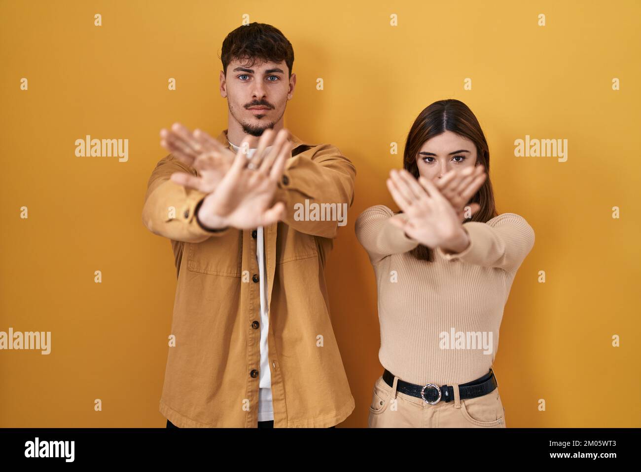 Young hispanic couple standing over yellow background rejection ...
