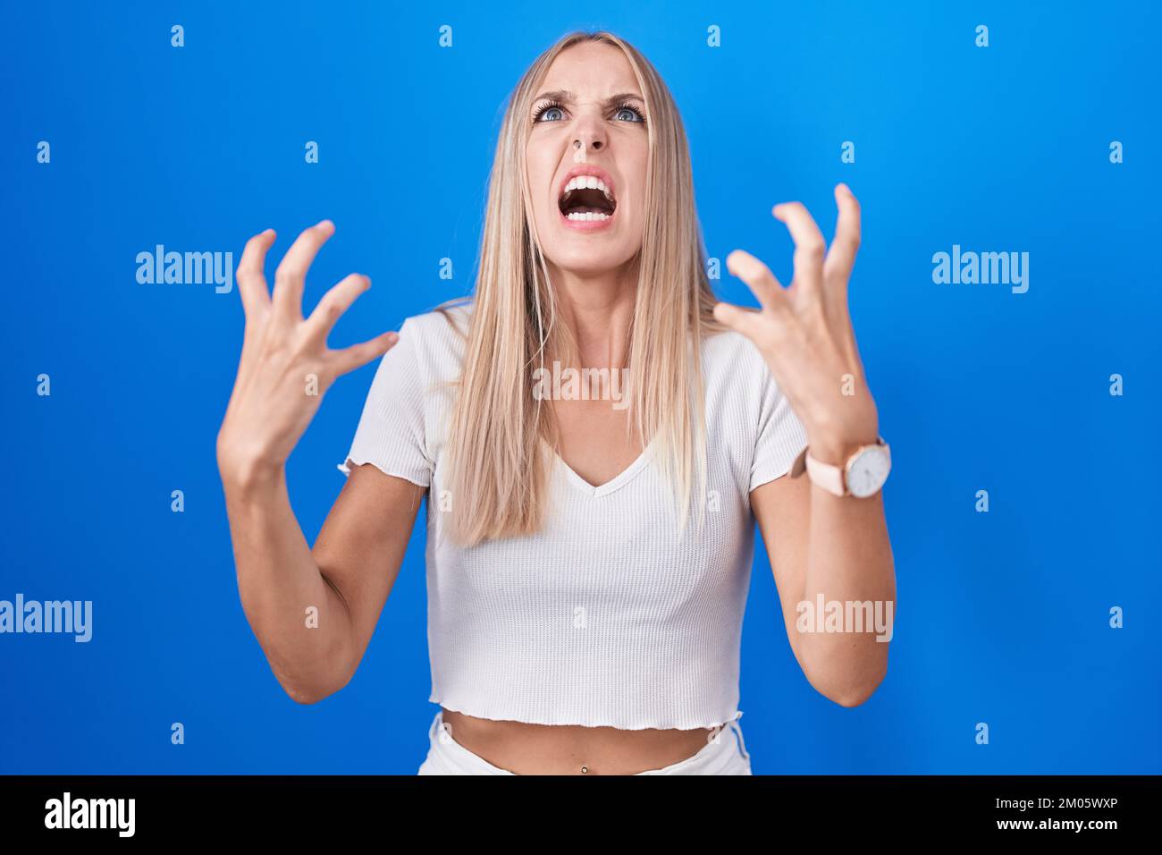 Young caucasian woman standing over blue background crazy and mad ...