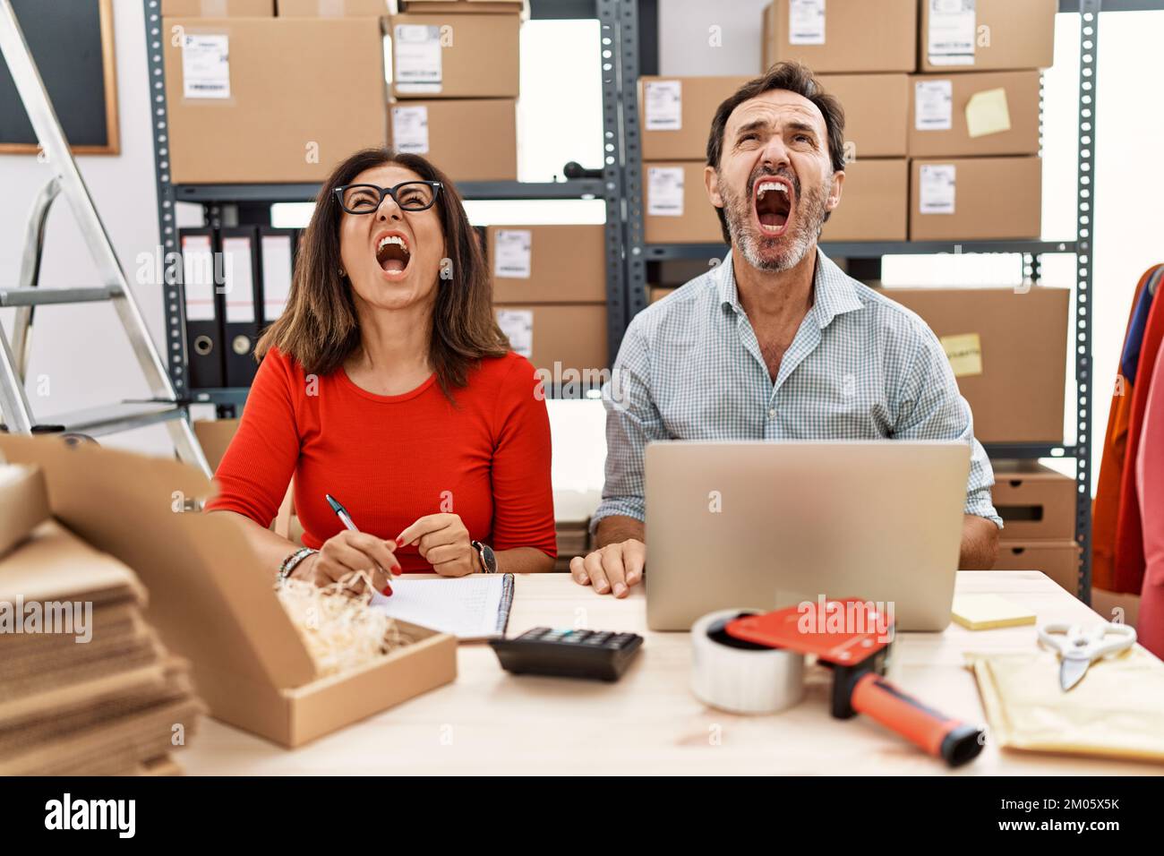 Middle age couple working at small business ecommerce angry and mad screaming frustrated and ...