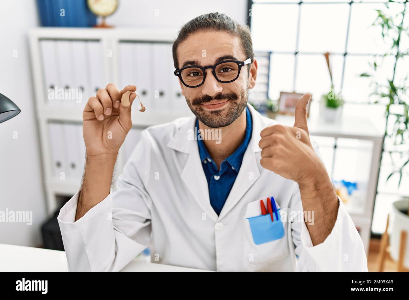 Young hispanic doctor man holding medical hearing aid smiling happy and ...