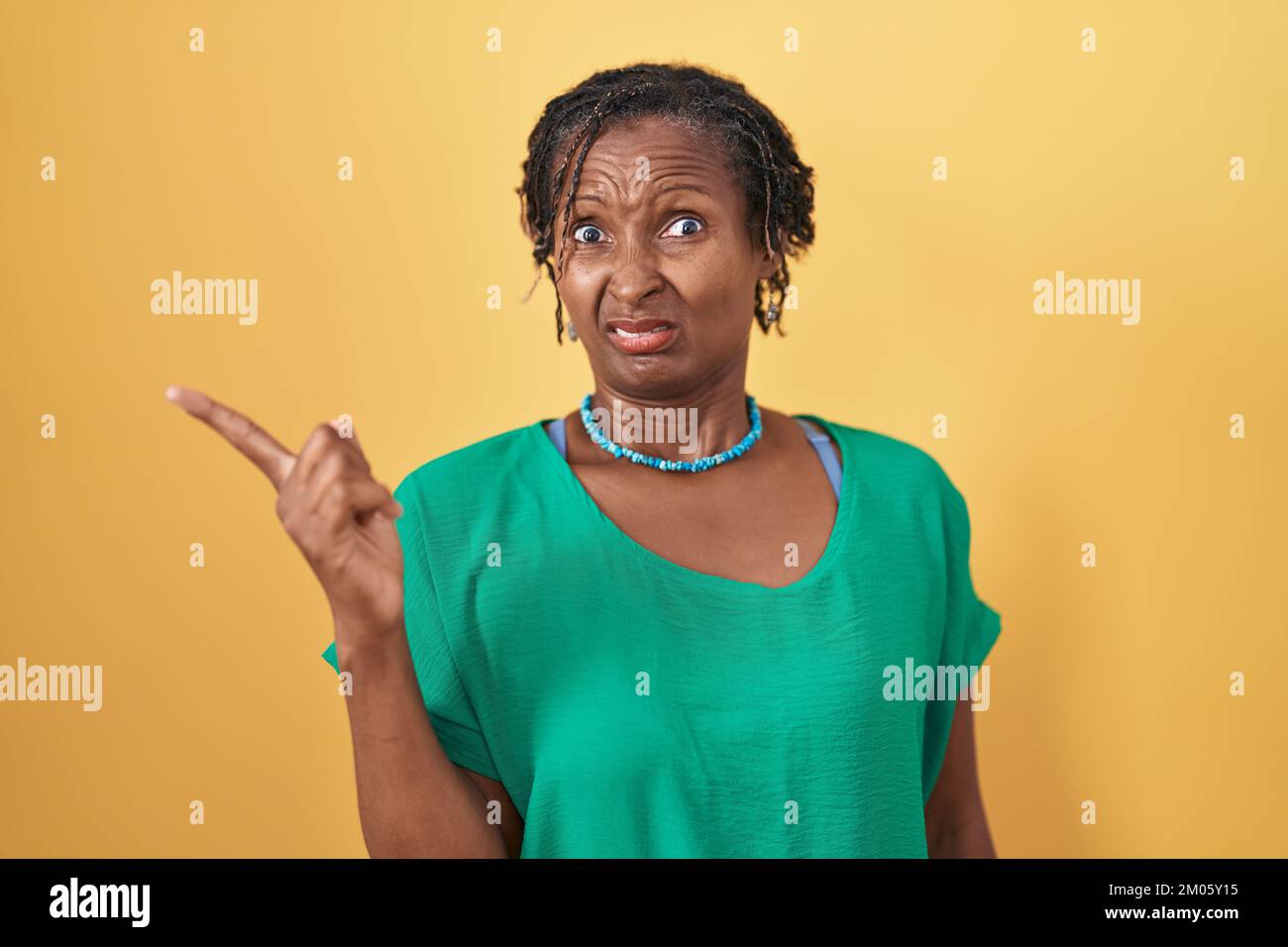 African woman with dreadlocks standing over yellow background pointing ...