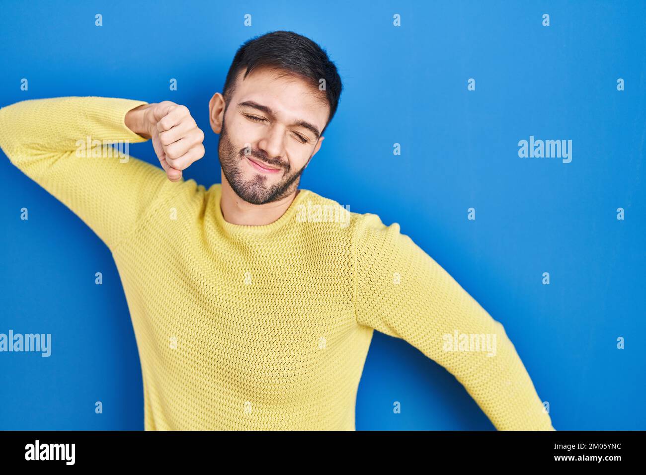 Hispanic man standing over blue background stretching back, tired and ...