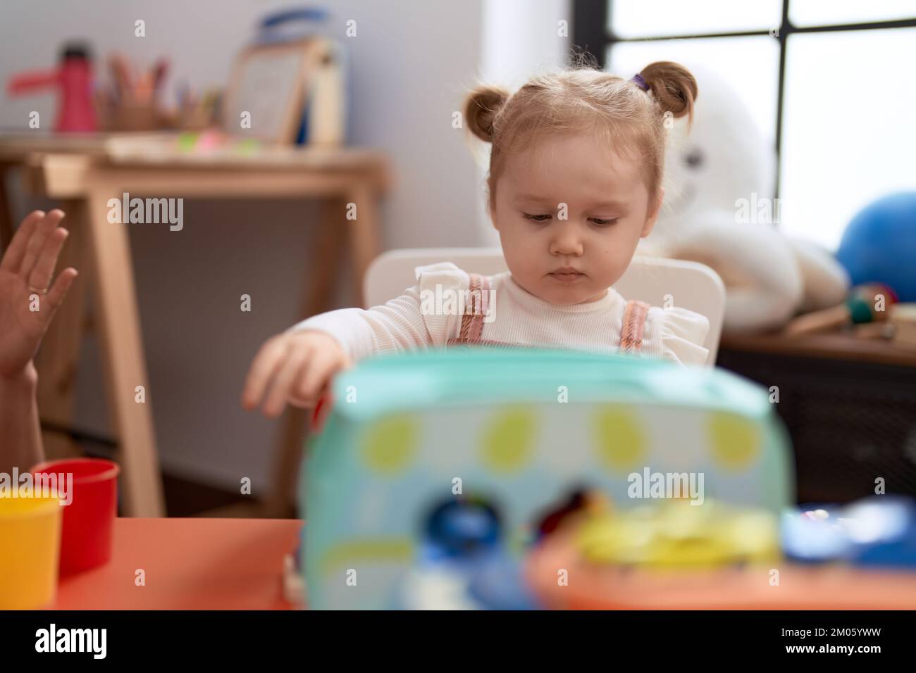 Adorable caucasian girl playing with truck toy sitting on table at ...