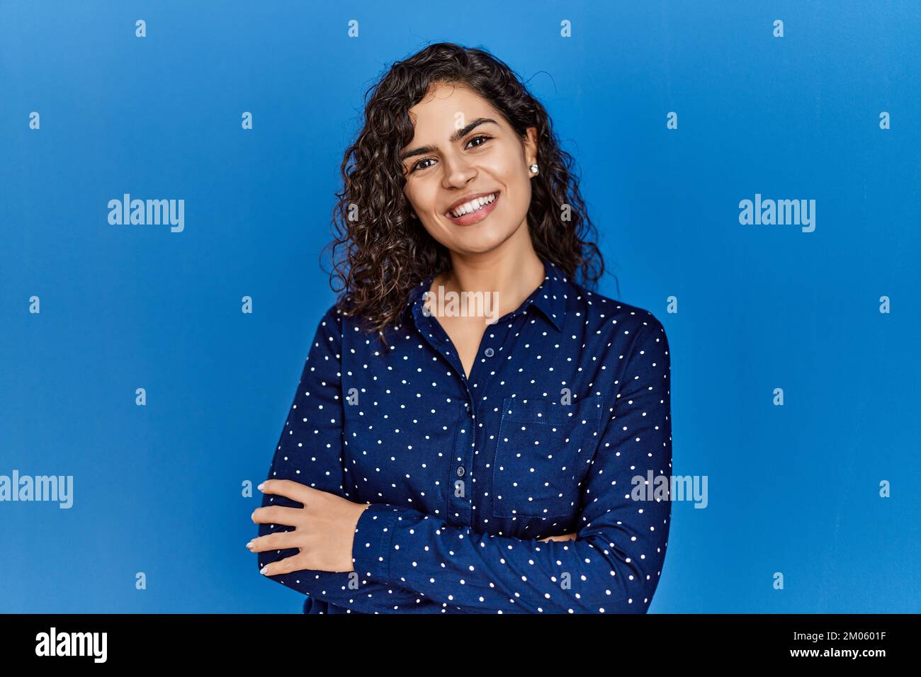 Young brunette woman with curly hair wearing casual clothes over blue ...
