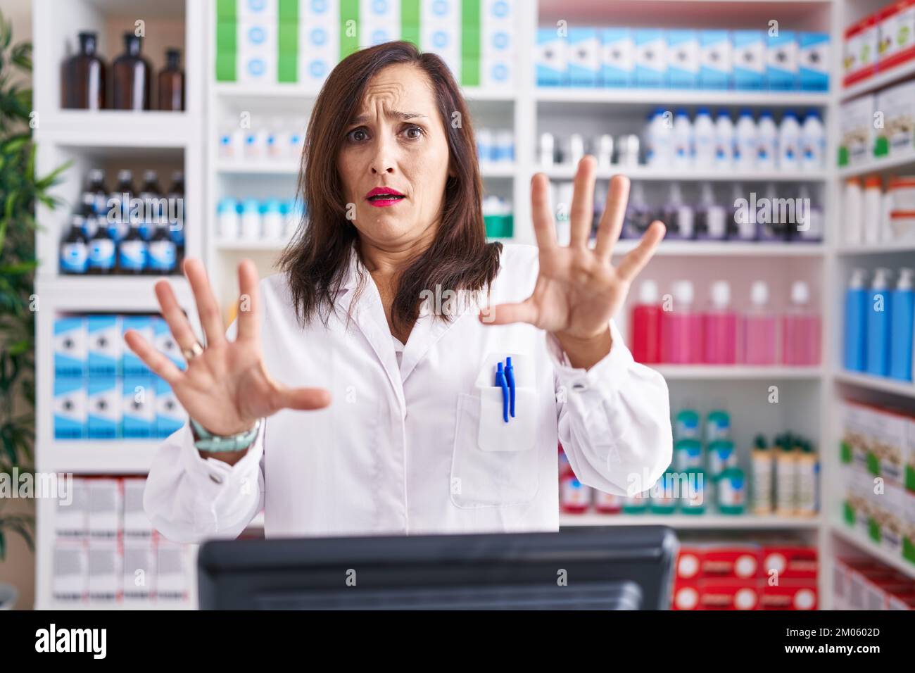Middle age brunette woman working at pharmacy drugstore afraid and ...