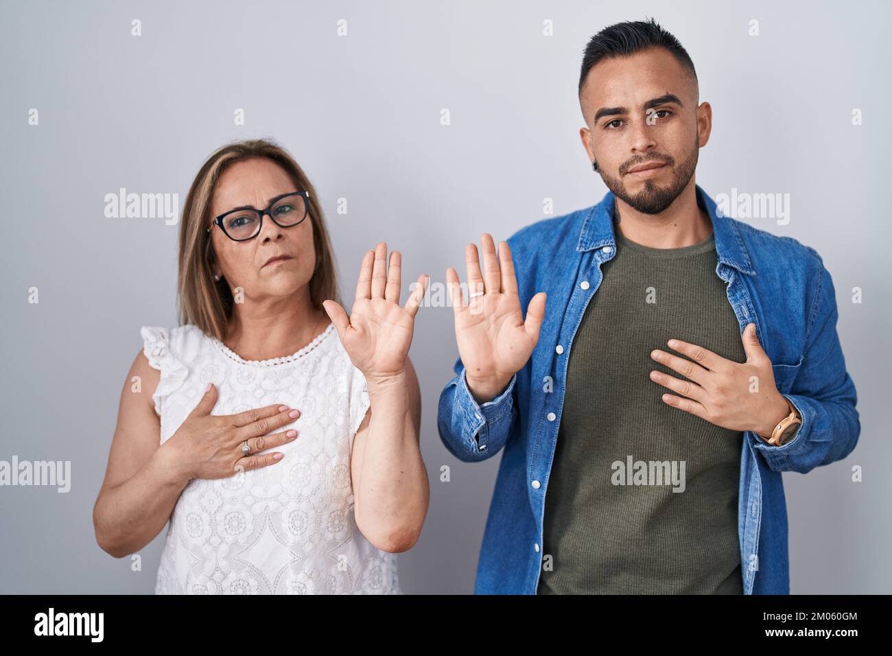 Hispanic mother and son standing together swearing with hand on chest ...
