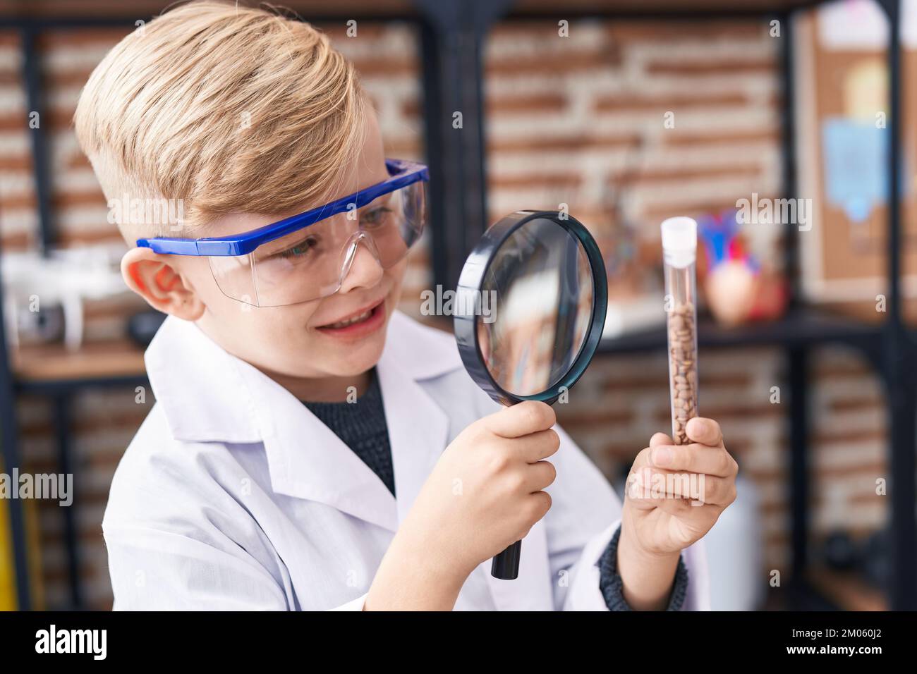 Adorable toddler student looking test tube with loupe at classroom ...