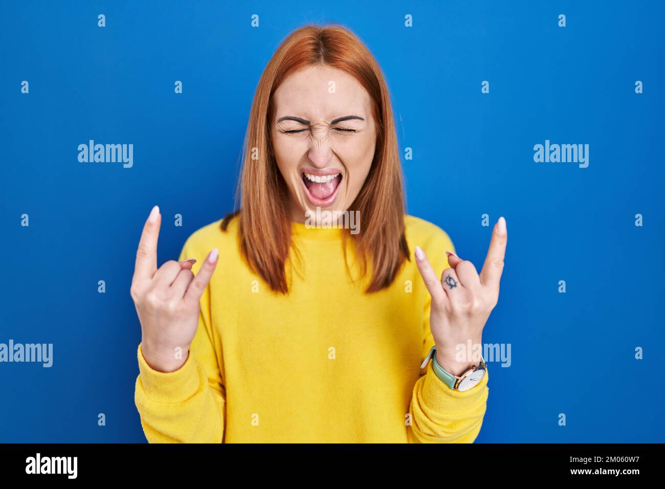 Young woman standing over blue background shouting with crazy ...