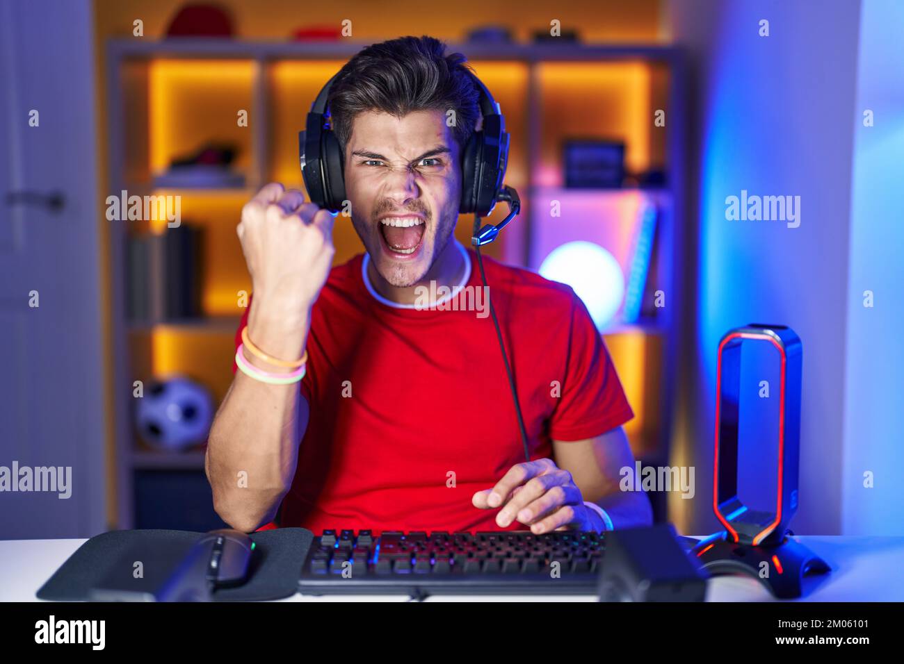 Young hispanic man playing video games angry and mad raising fist ...