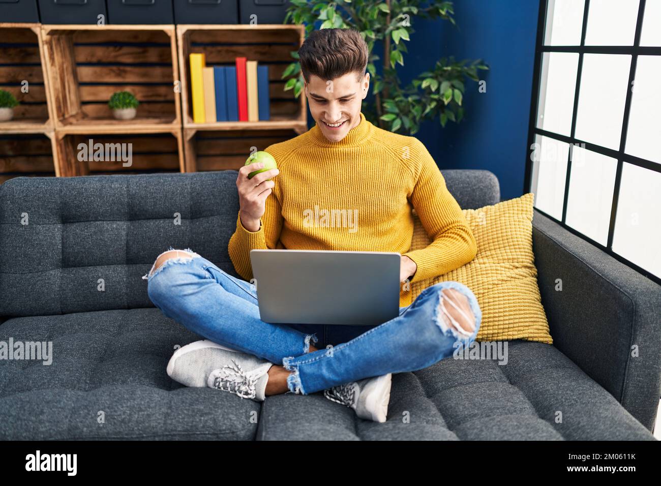 Young hispanic man using laptop eating apple at home Stock Photo - Alamy