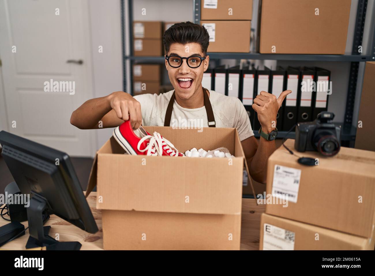 Young hispanic man working at small business ecommerce pointing thumb ...