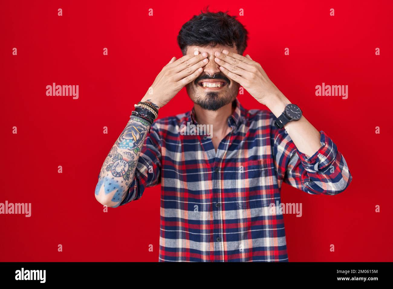 Young hispanic man with beard standing over red background covering ...