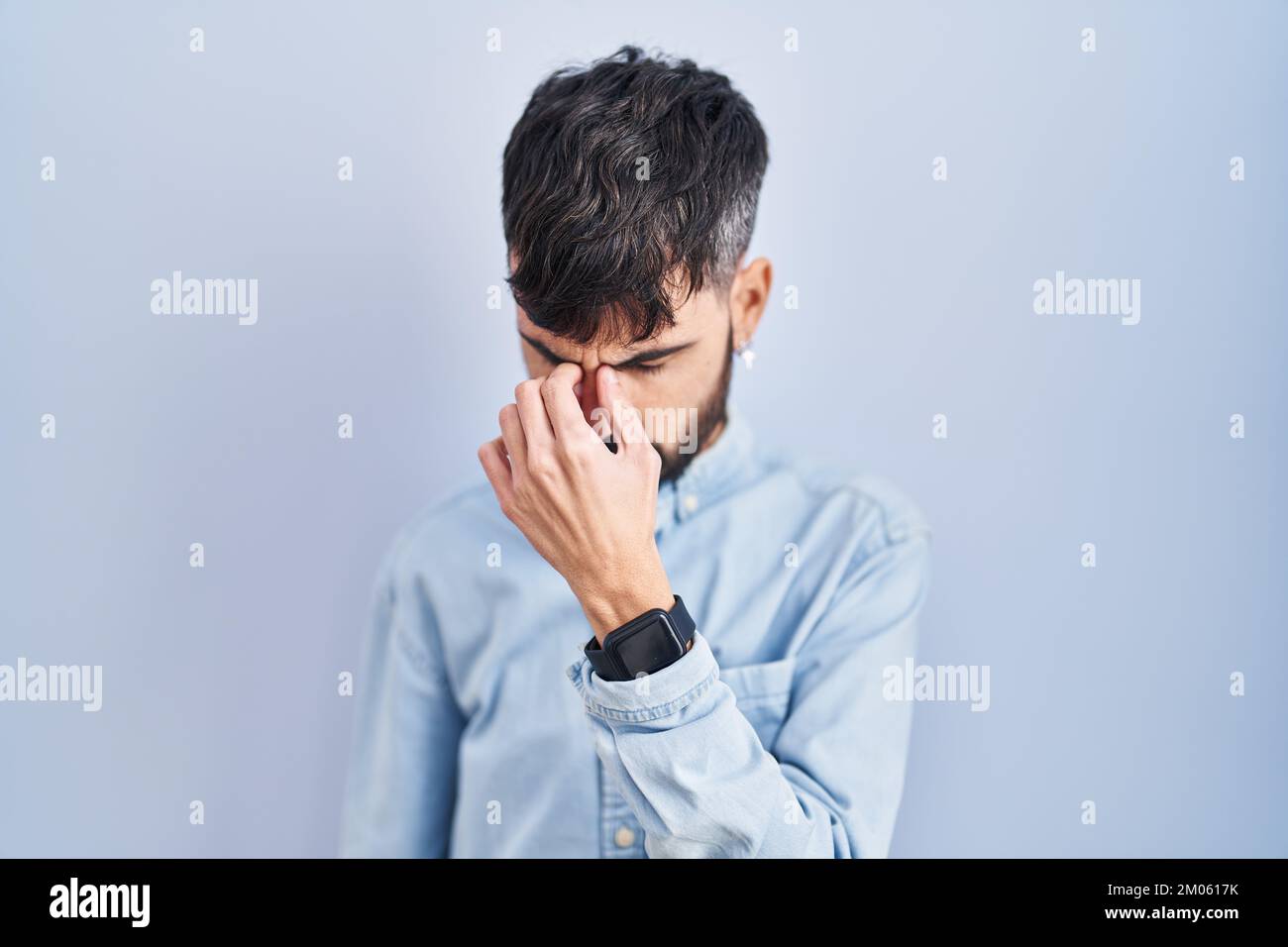 Young hispanic man with beard standing over blue background tired ...