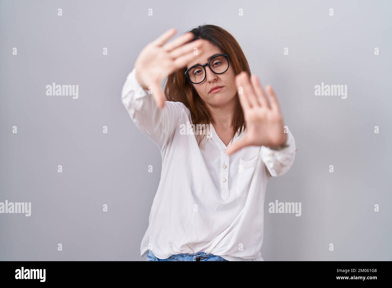 Brunette woman standing over white isolated background doing frame ...