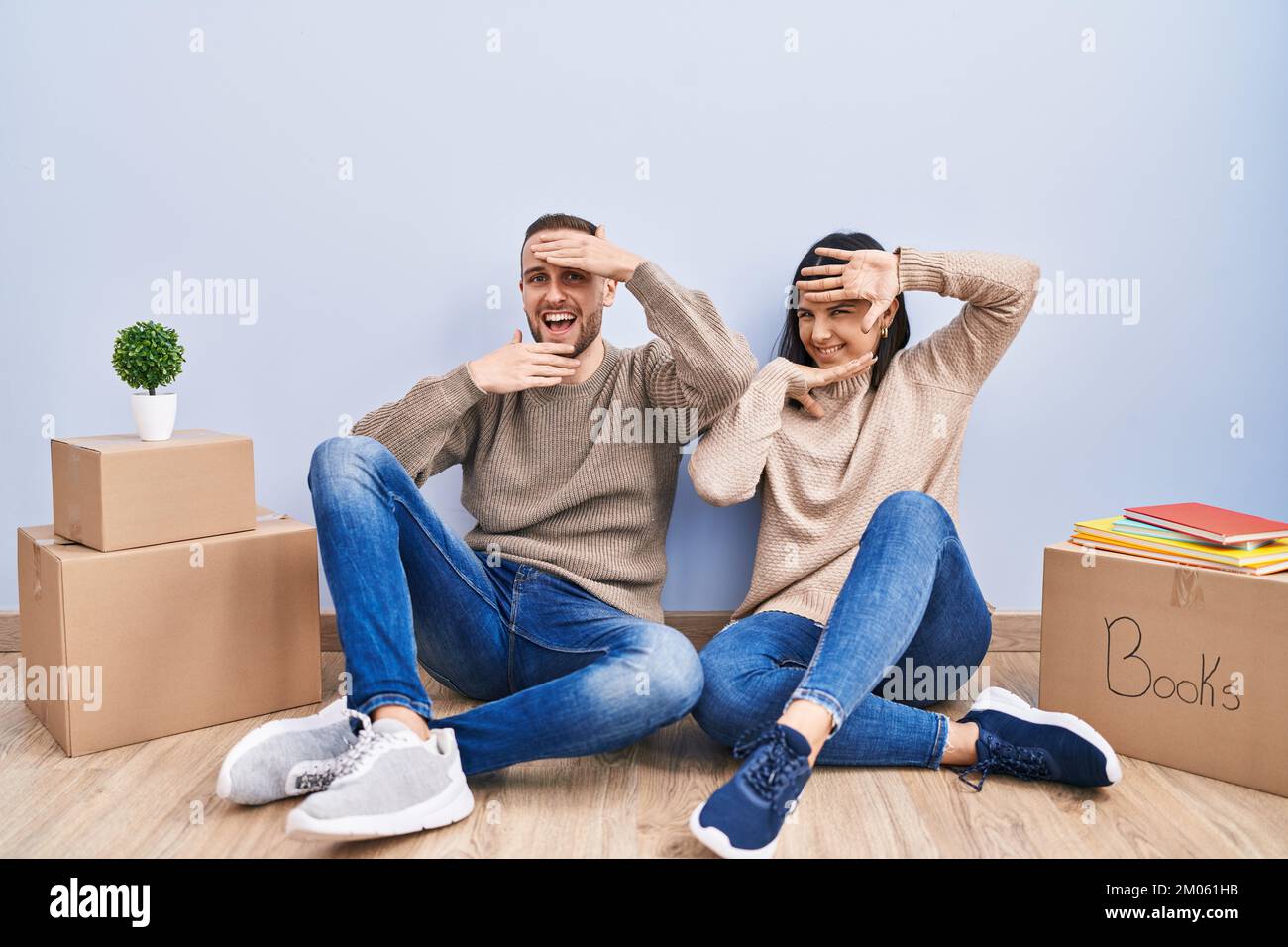 Young couple moving to a new home smiling cheerful playing peek a boo ...