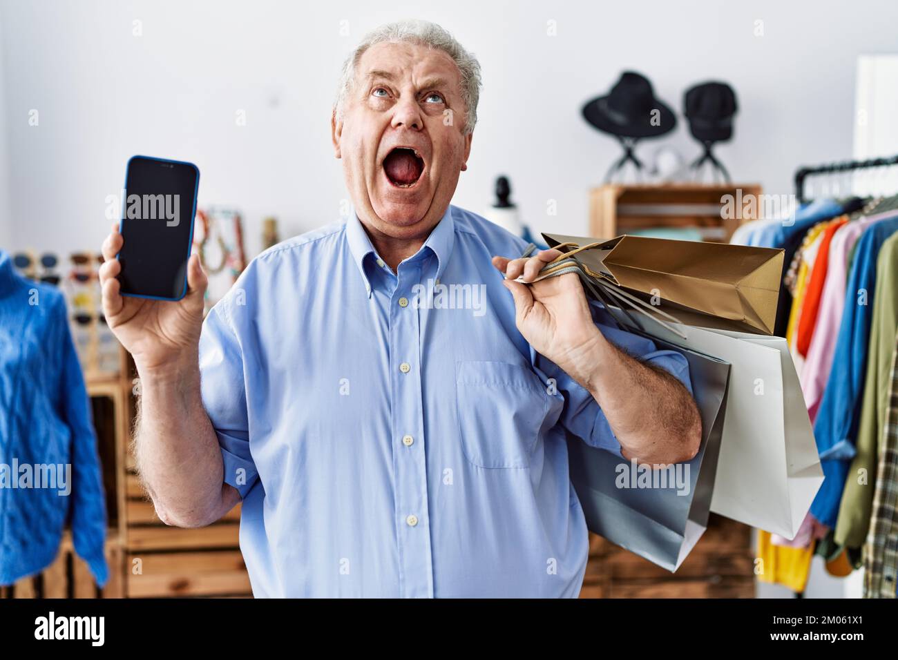 Senior man with grey hair holding shopping bags and showing smartphone ...