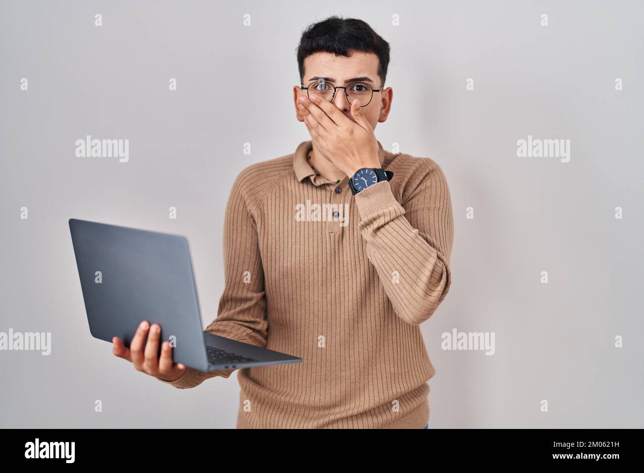 Non binary person using computer laptop shocked covering mouth with ...