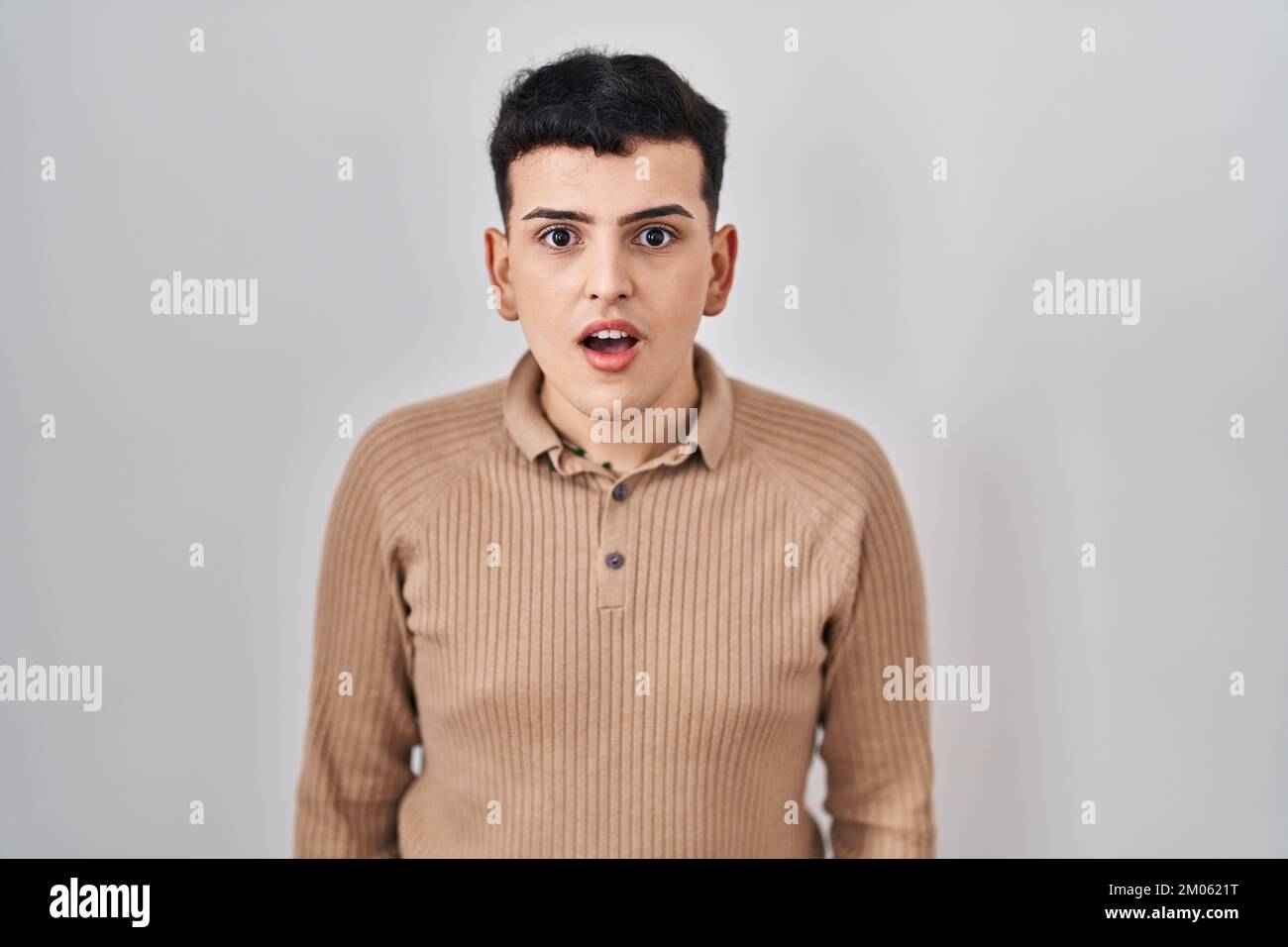 Non binary person standing over isolated background afraid and shocked ...